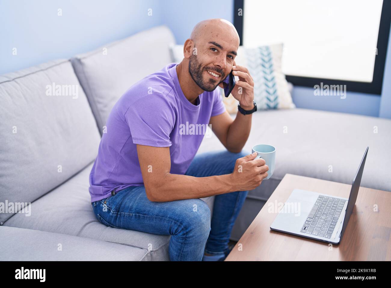 Young bald man talking on smartphone drinking coffee at home Stock ...