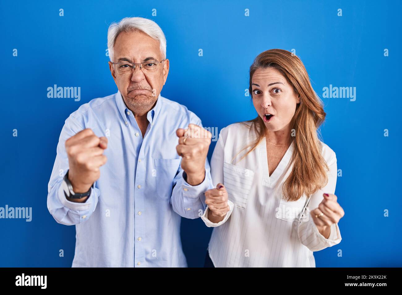 Middle age hispanic couple standing over blue background angry and mad ...