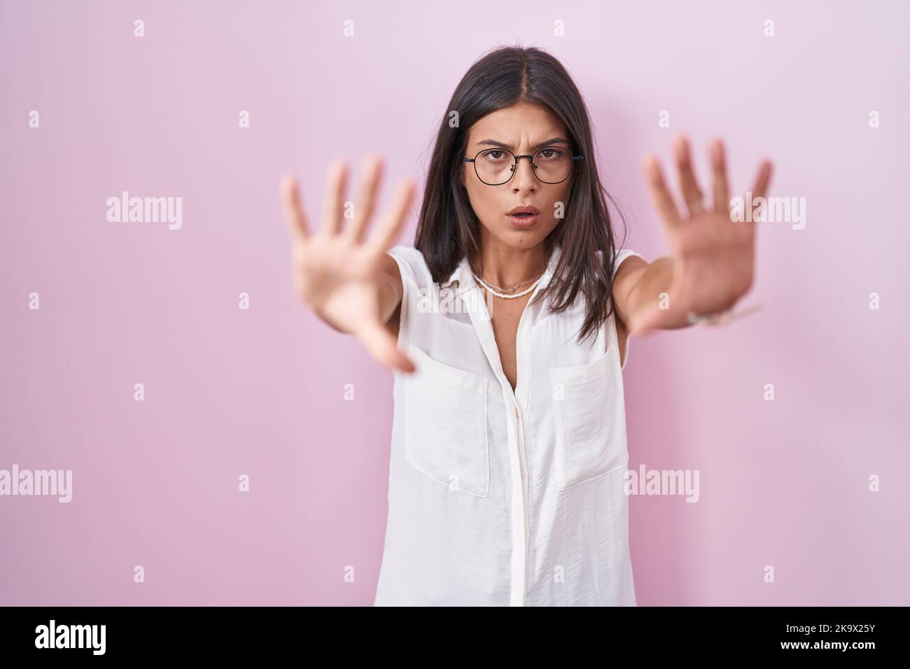 Brunette young woman standing over pink background wearing glasses ...