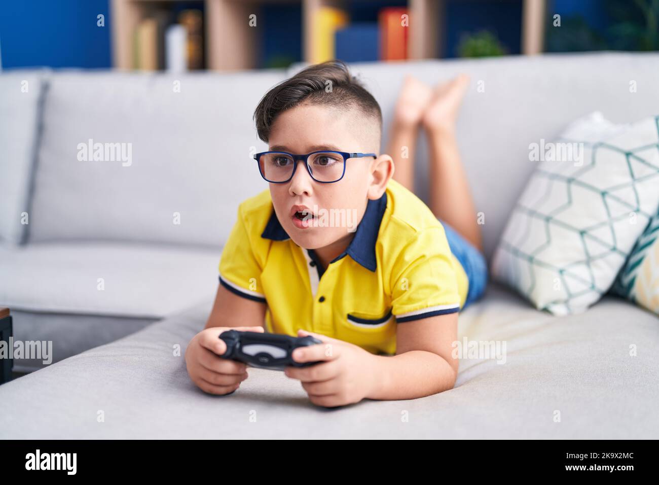 Young hispanic kid playing video game holding controller on the sofa in ...