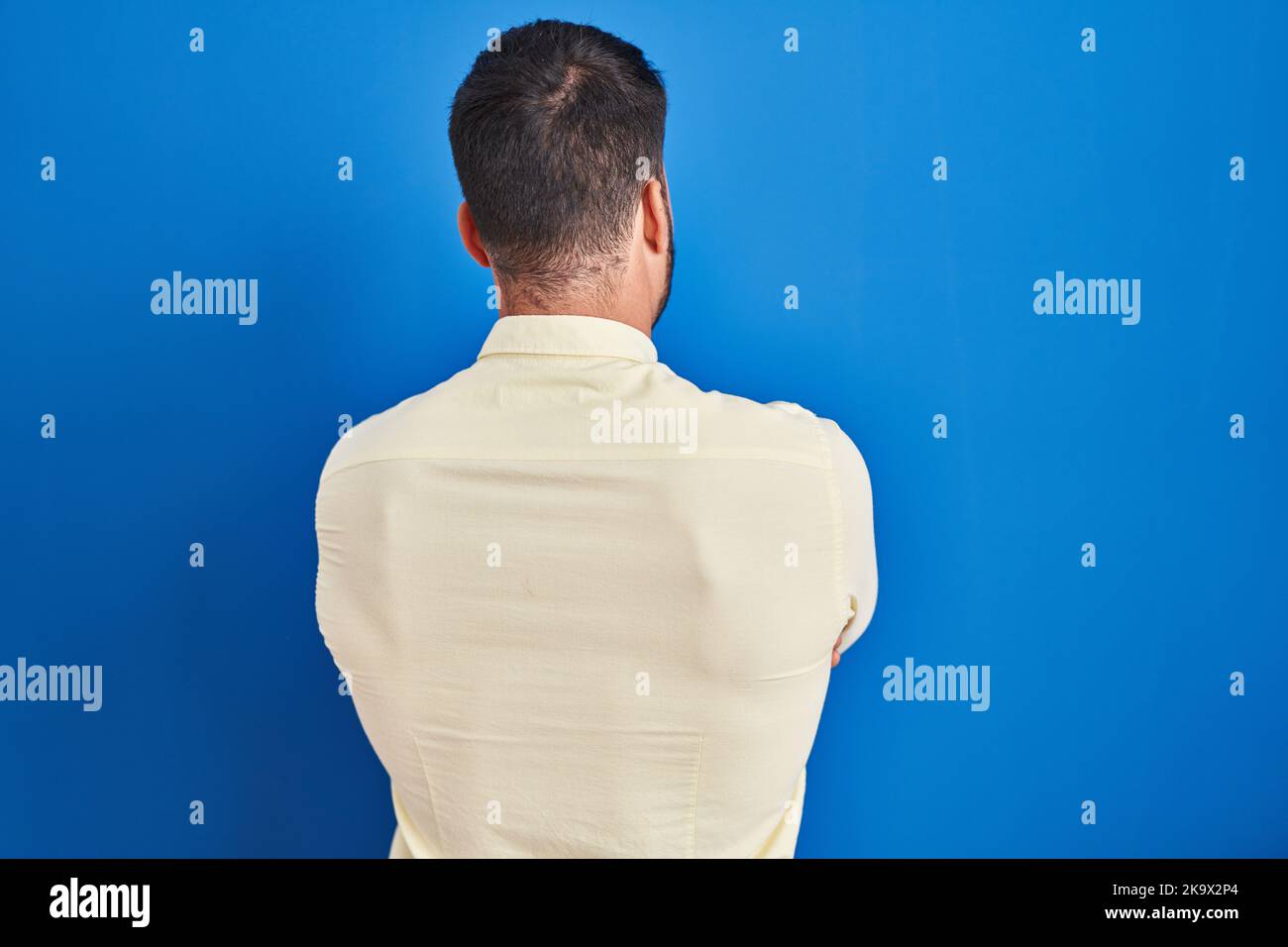 Handsome hispanic man standing over blue background standing backwards ...