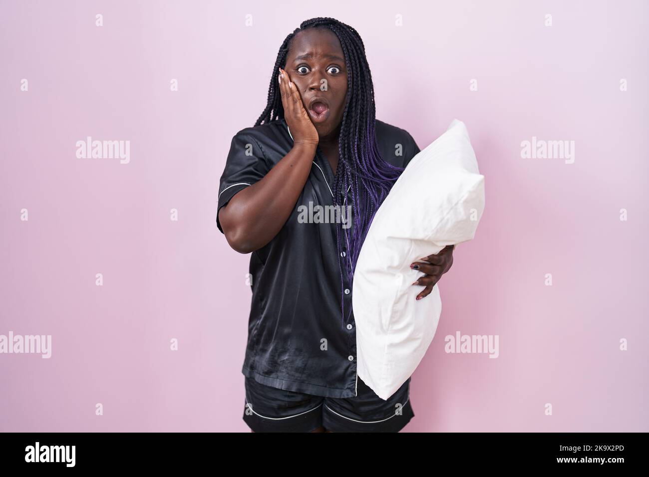 Young african woman wearing pijama hugging pillow afraid and shocked ...