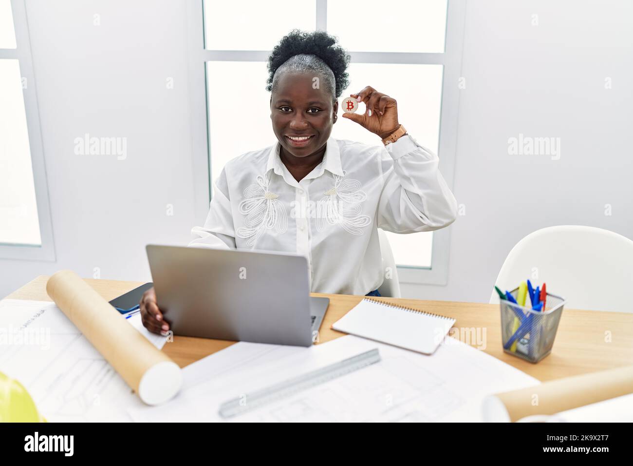 Young african american woman architect using laptop holding bitcoin at ...