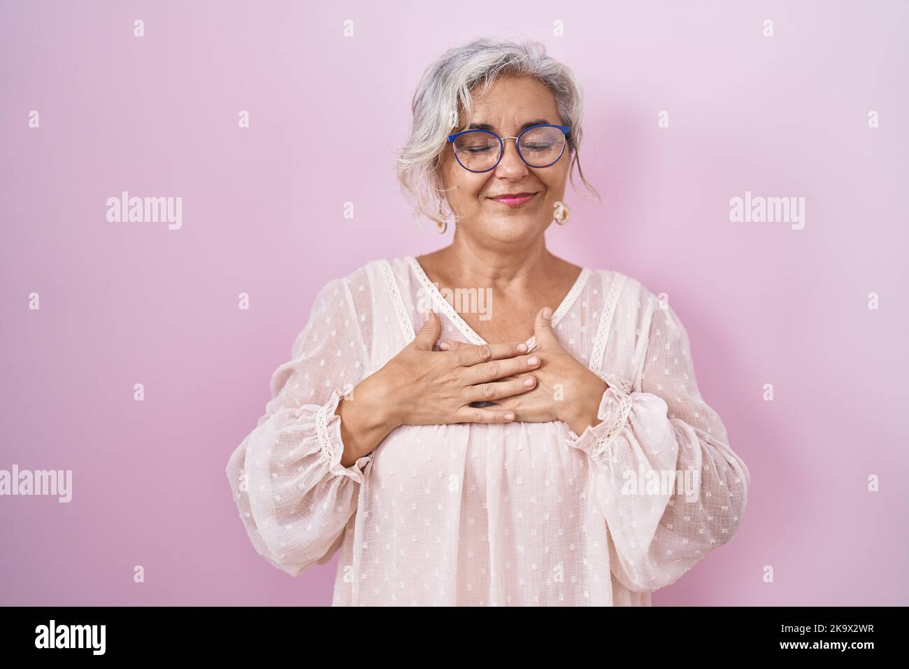 Middle age woman with grey hair standing over pink background smiling ...