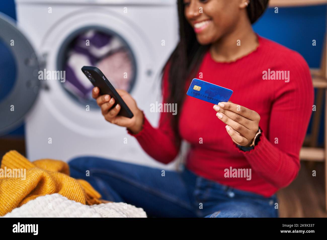 African american woman using smartphone and credit card washing clothes ...