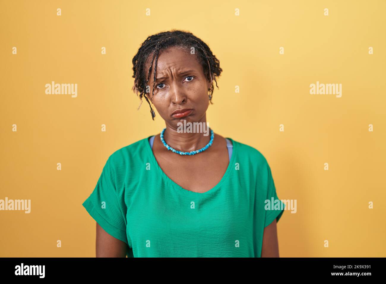 African woman with dreadlocks standing over yellow background depressed ...
