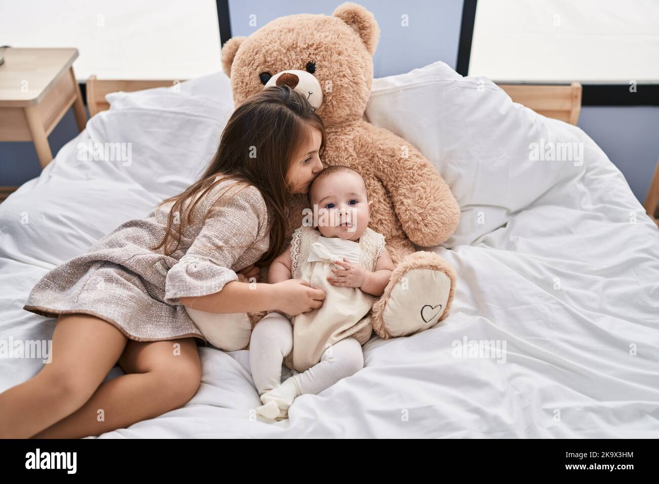 Brother and sister kissing and lying together with teddy bear on bed at ...