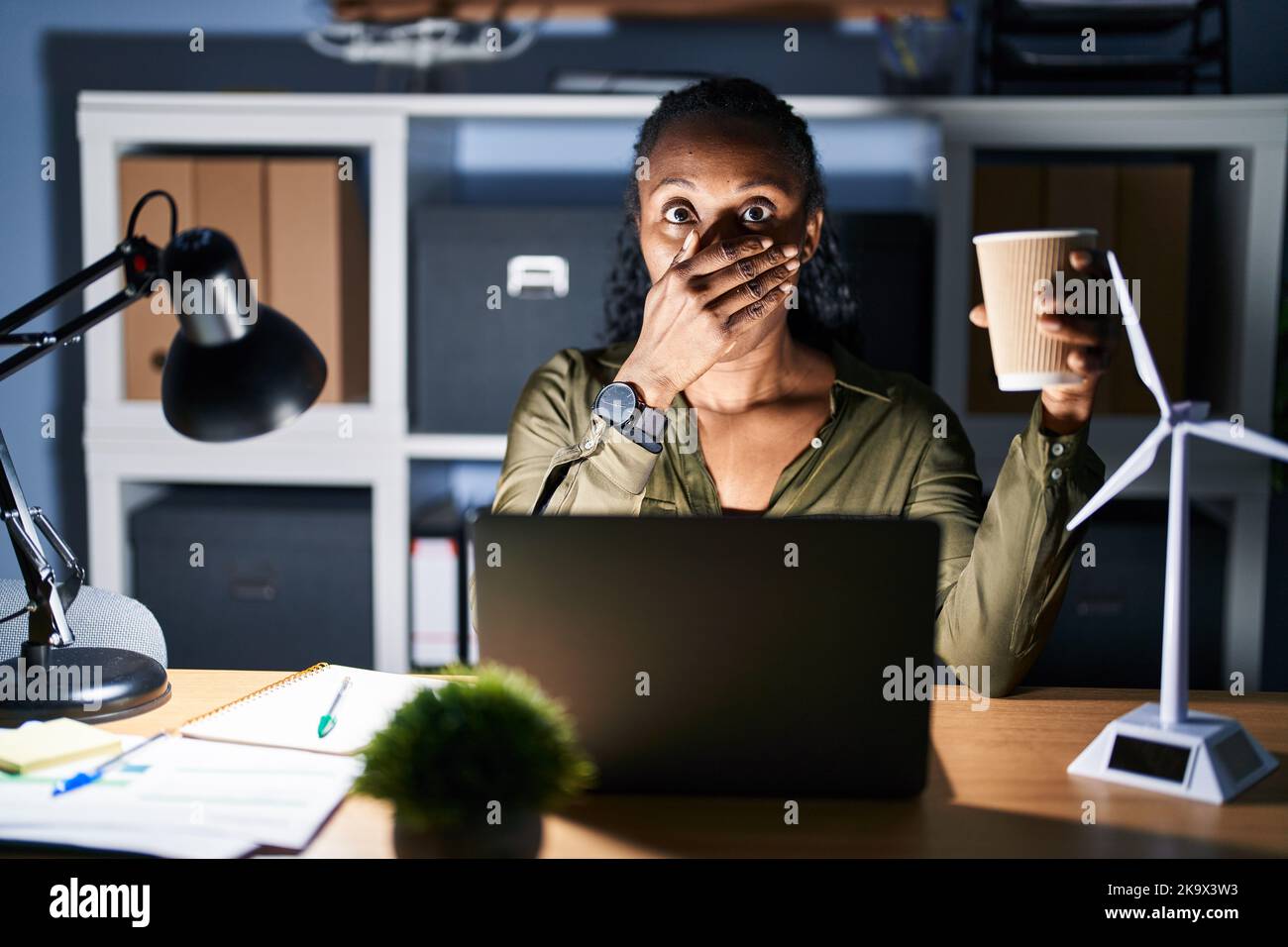 African woman working using computer laptop at night shocked covering ...
