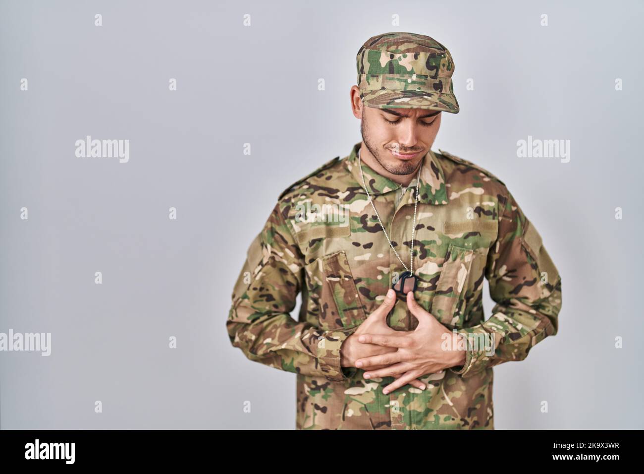 Young hispanic man wearing camouflage army uniform with hand on stomach ...