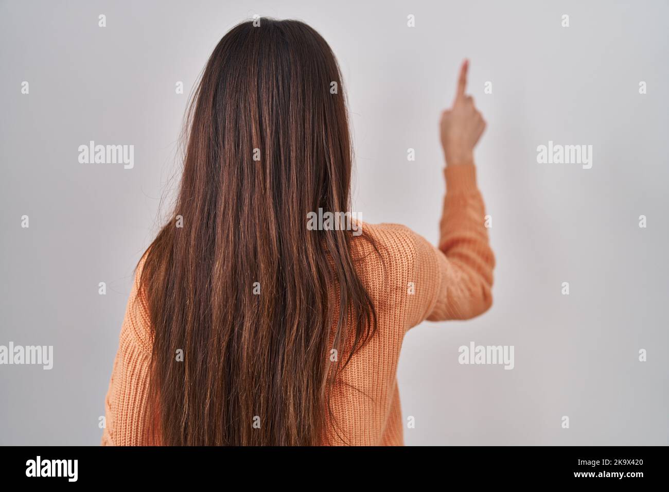 Young brunette woman standing over white background posing backwards ...