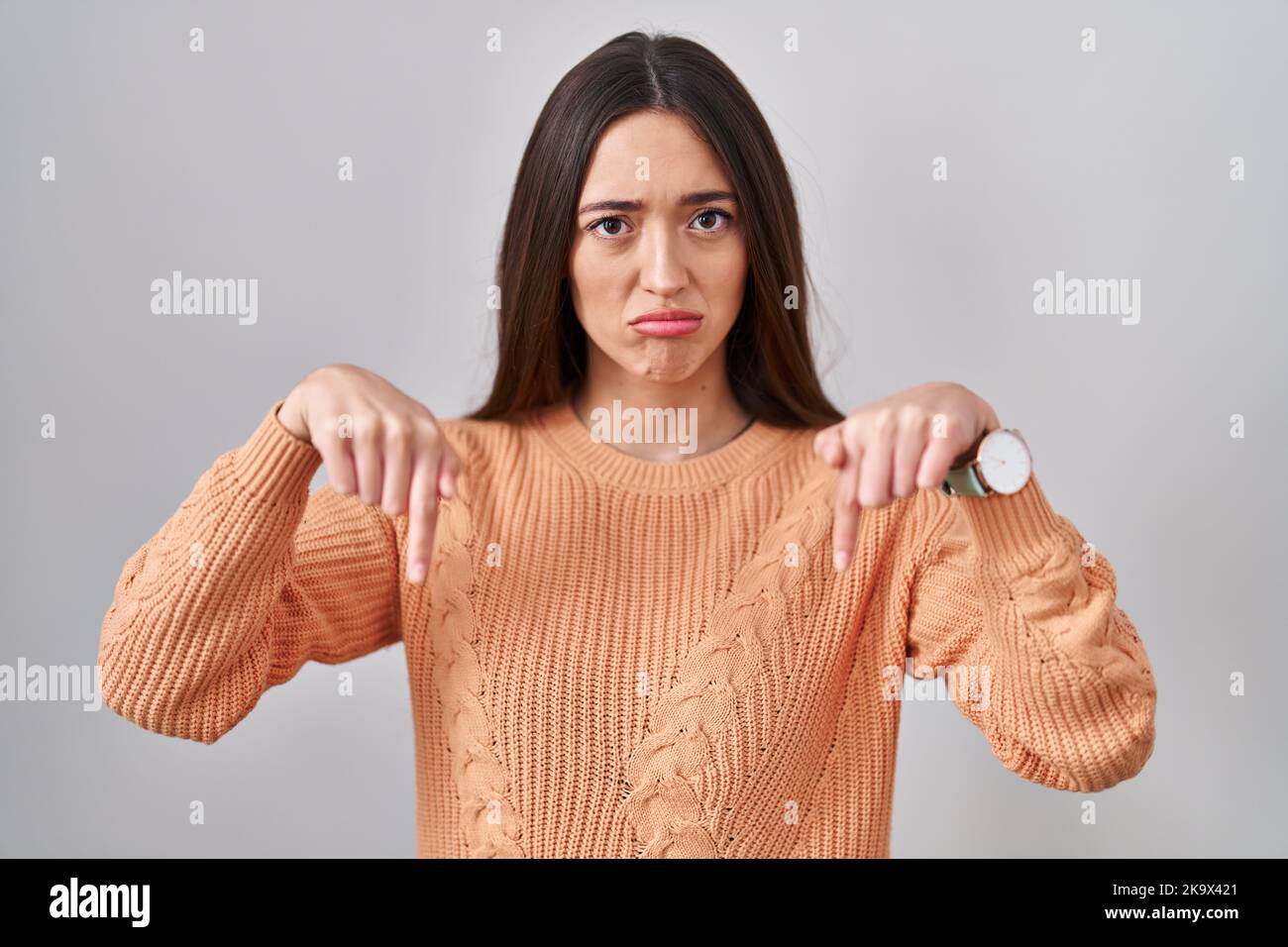 Young brunette woman standing over white background pointing down ...