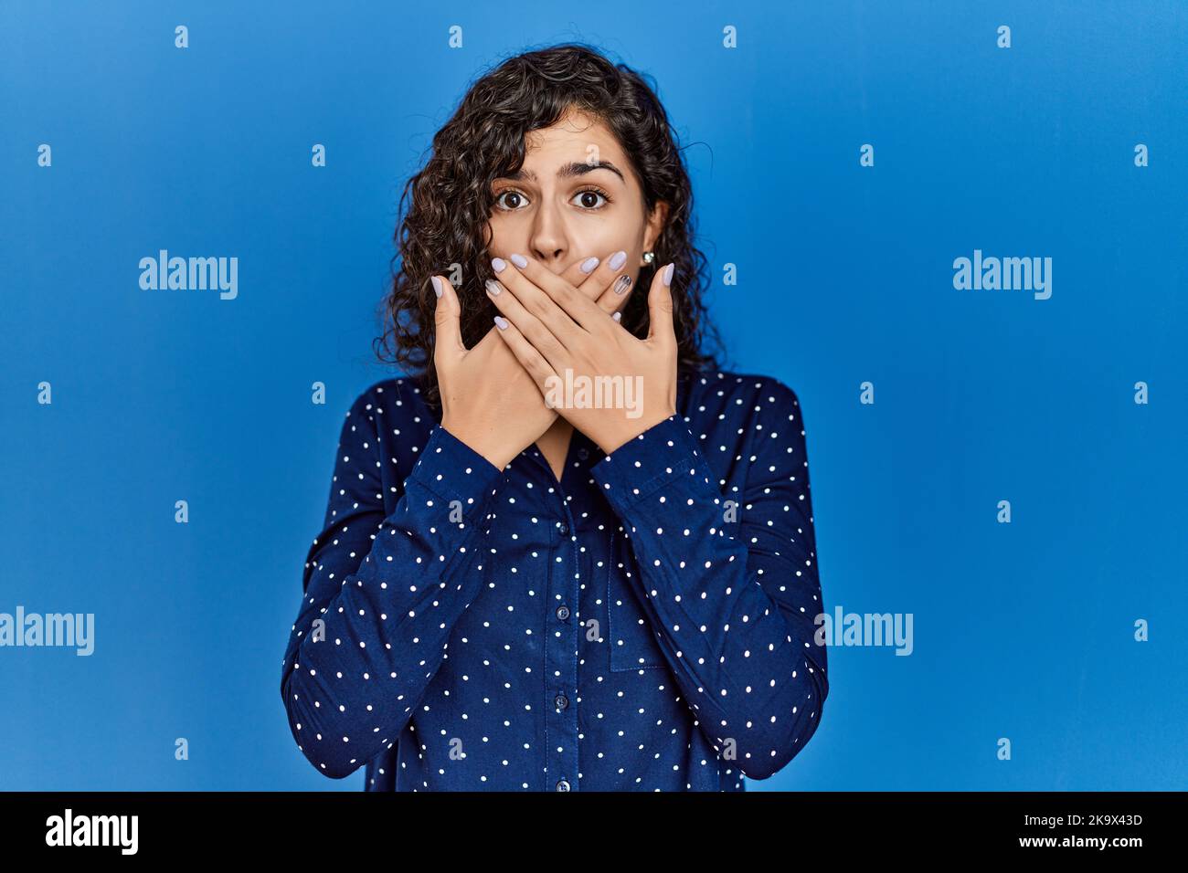 Young brunette woman with curly hair wearing casual clothes over blue ...
