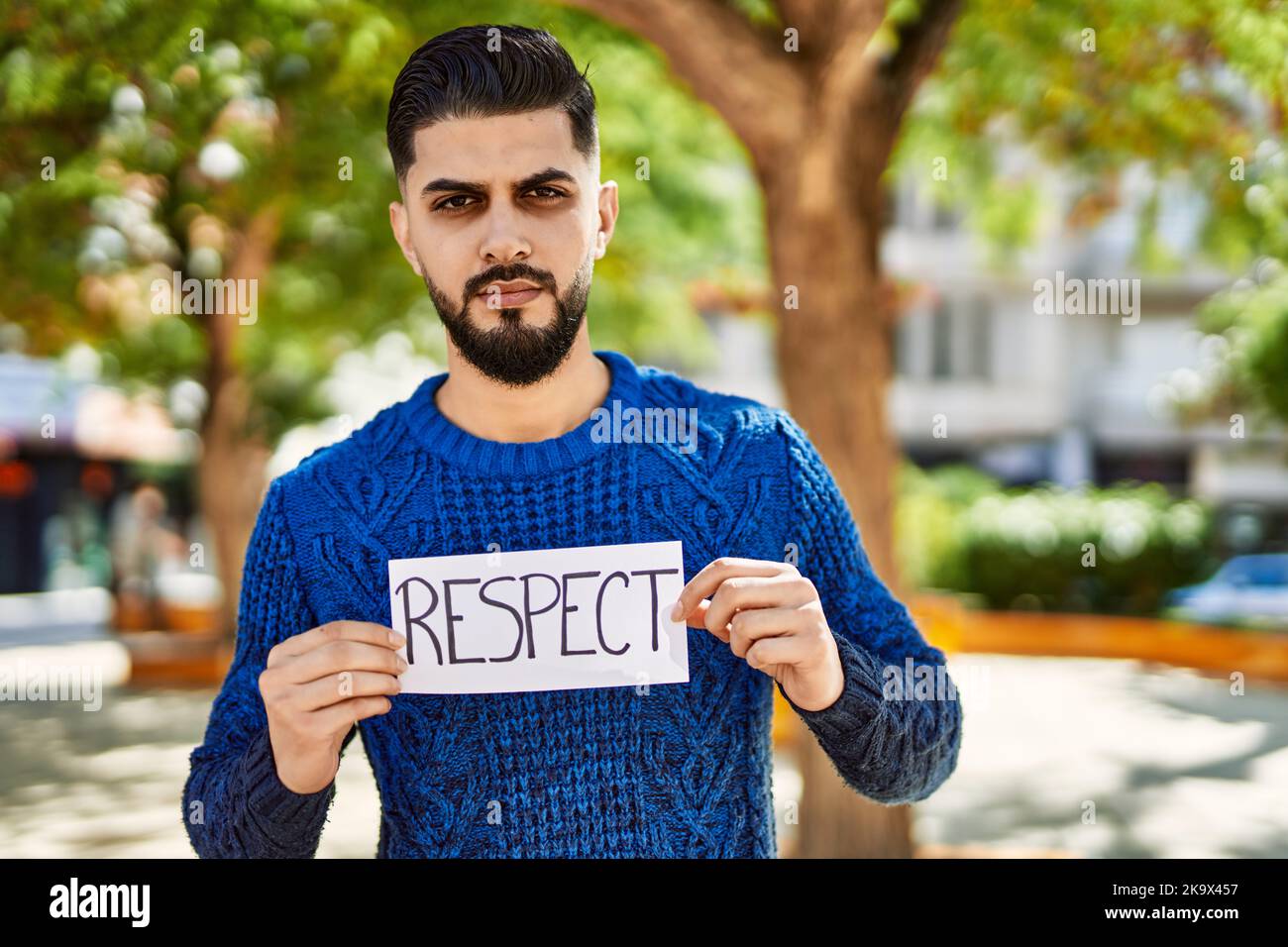 Young arab man serious holding respect banner at park Stock Photo - Alamy
