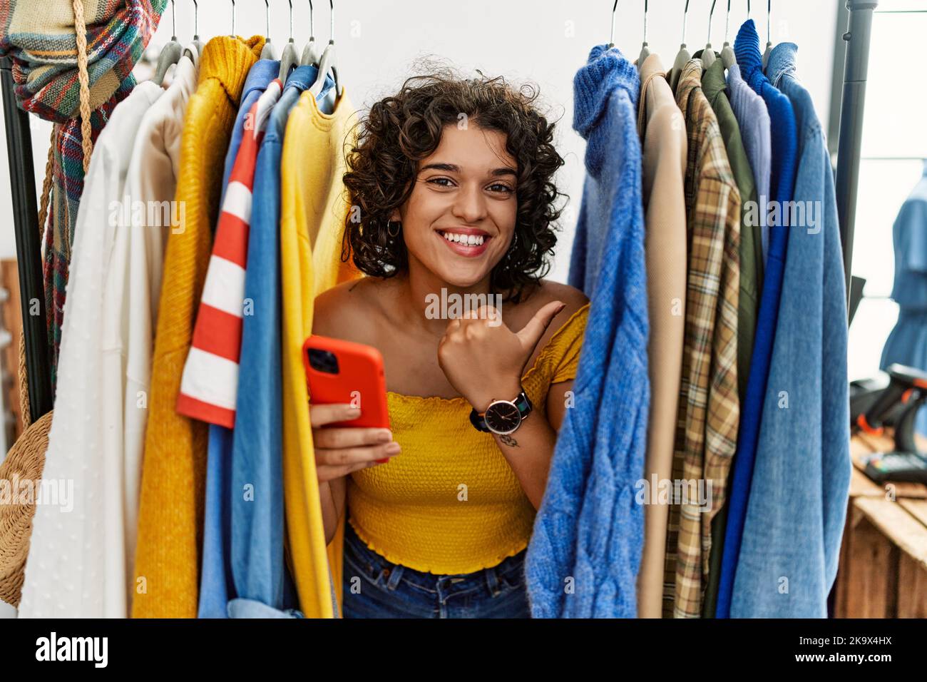 Young hispanic woman searching clothes on clothing rack using ...