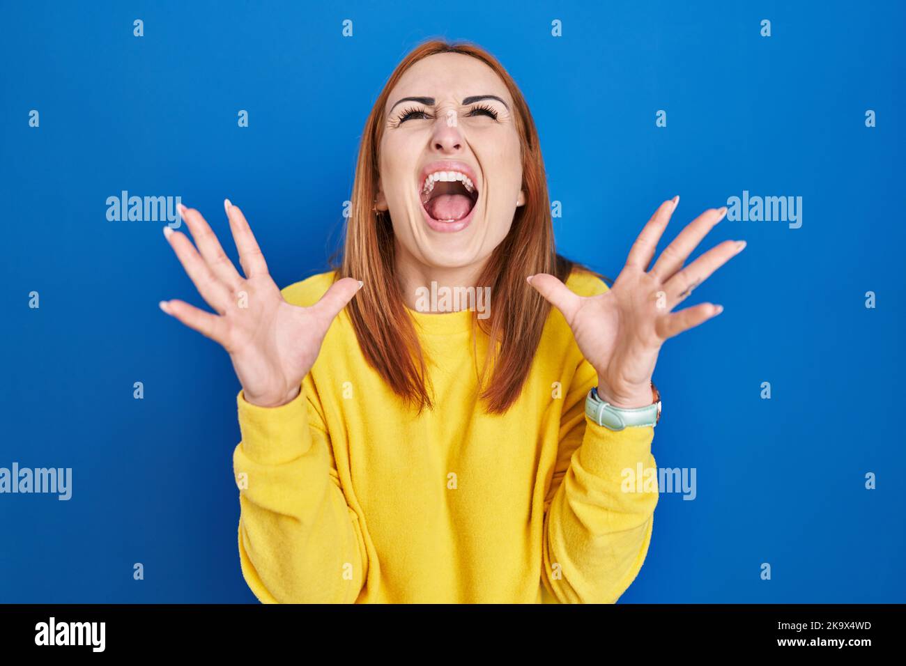 Young woman standing over blue background crazy and mad shouting and ...