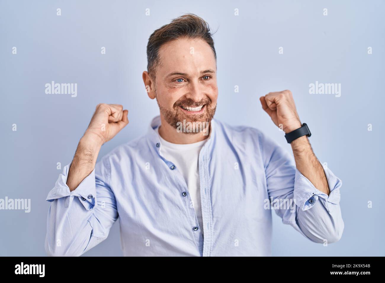 Middle age caucasian man standing over blue background celebrating ...