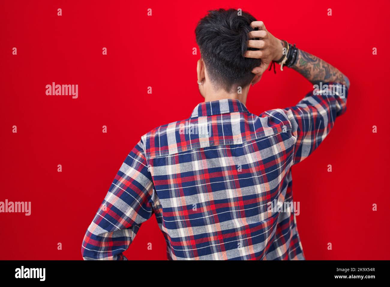 Young hispanic man with beard standing over red background backwards ...
