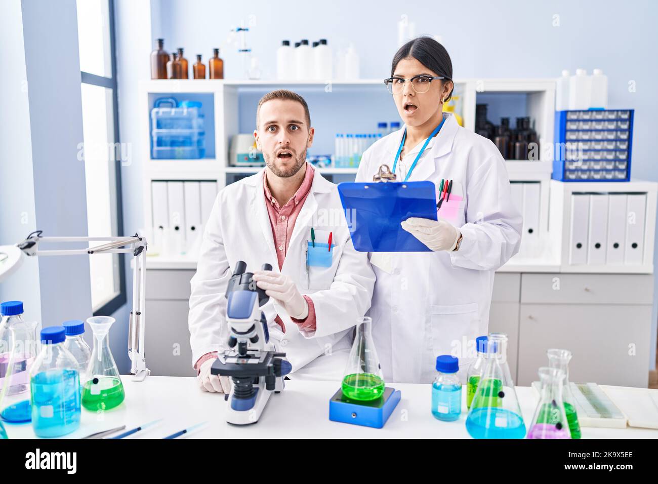 Two young people working at scientist laboratory scared and amazed with ...