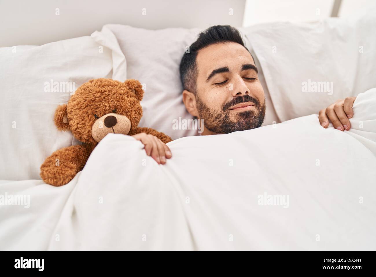 Young Hispanic Man Lying On Bed Sleeping With Teddy Bear At Bedroom