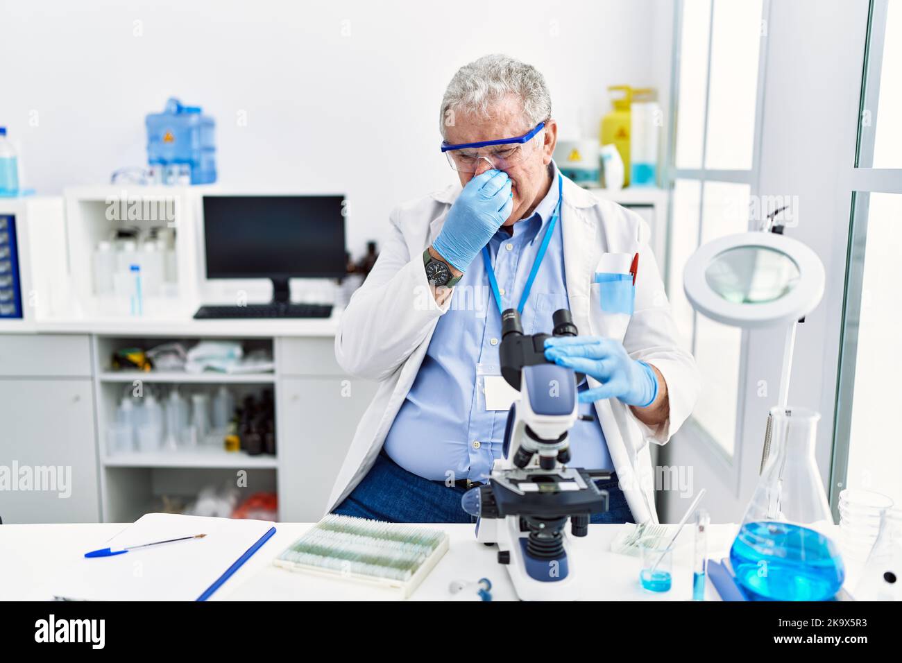 Senior caucasian man working at scientist laboratory smelling something ...