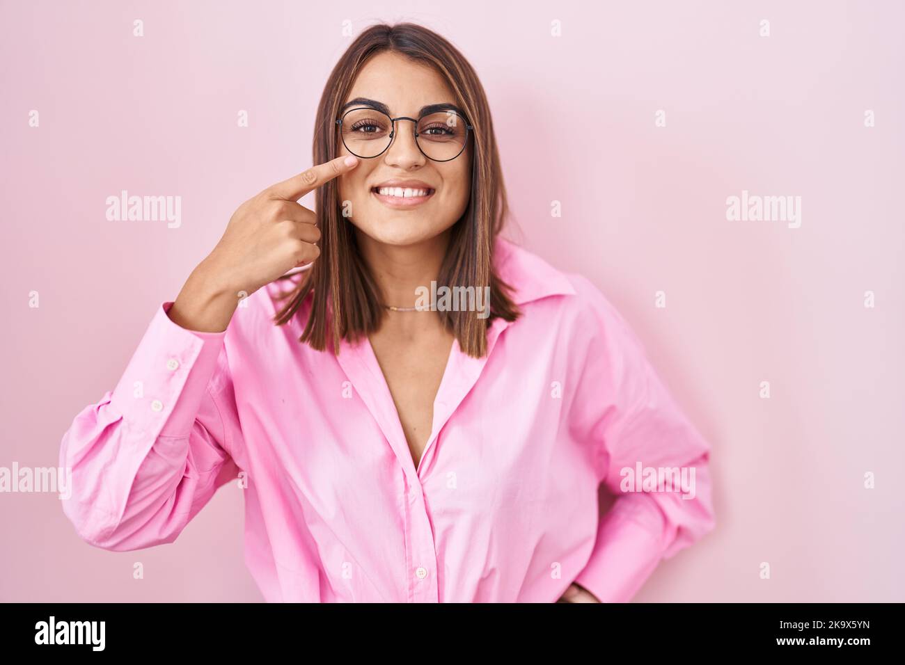 Young hispanic woman wearing glasses standing over pink background ...