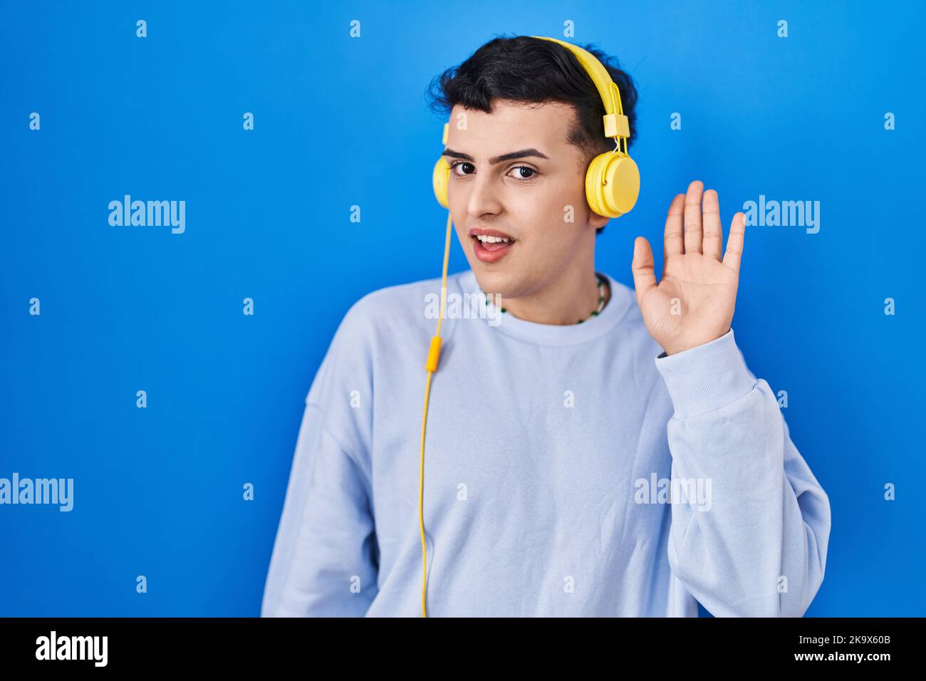 Non binary person listening to music using headphones waiving saying ...
