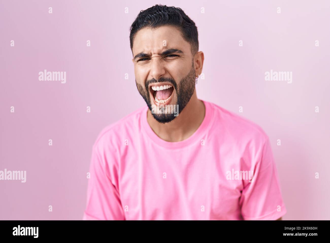 Hispanic young man standing over pink background angry and mad ...