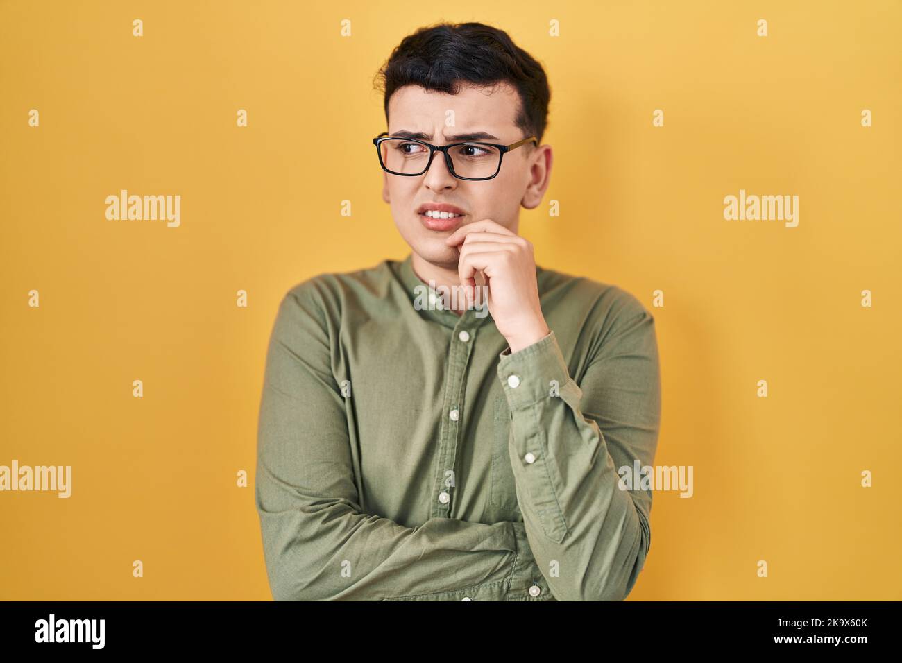 Non binary person standing over yellow background looking stressed and ...