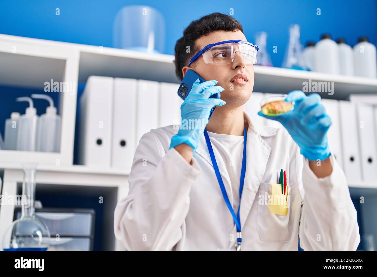 Young non binary man scientist talking on the smartphone holding sample at laboratory Stock ...