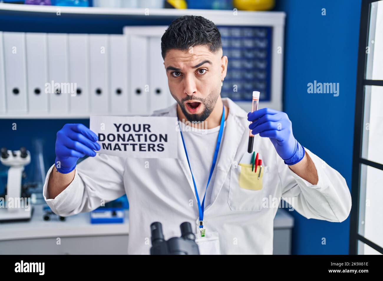 Young handsome man working at scientist laboratory holding blood sample ...