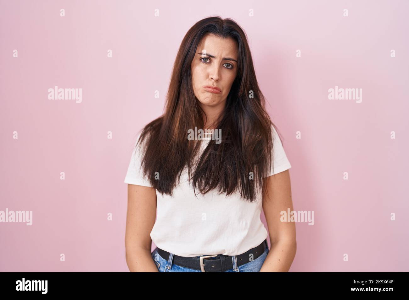 Young brunette woman standing over pink background depressed and worry ...