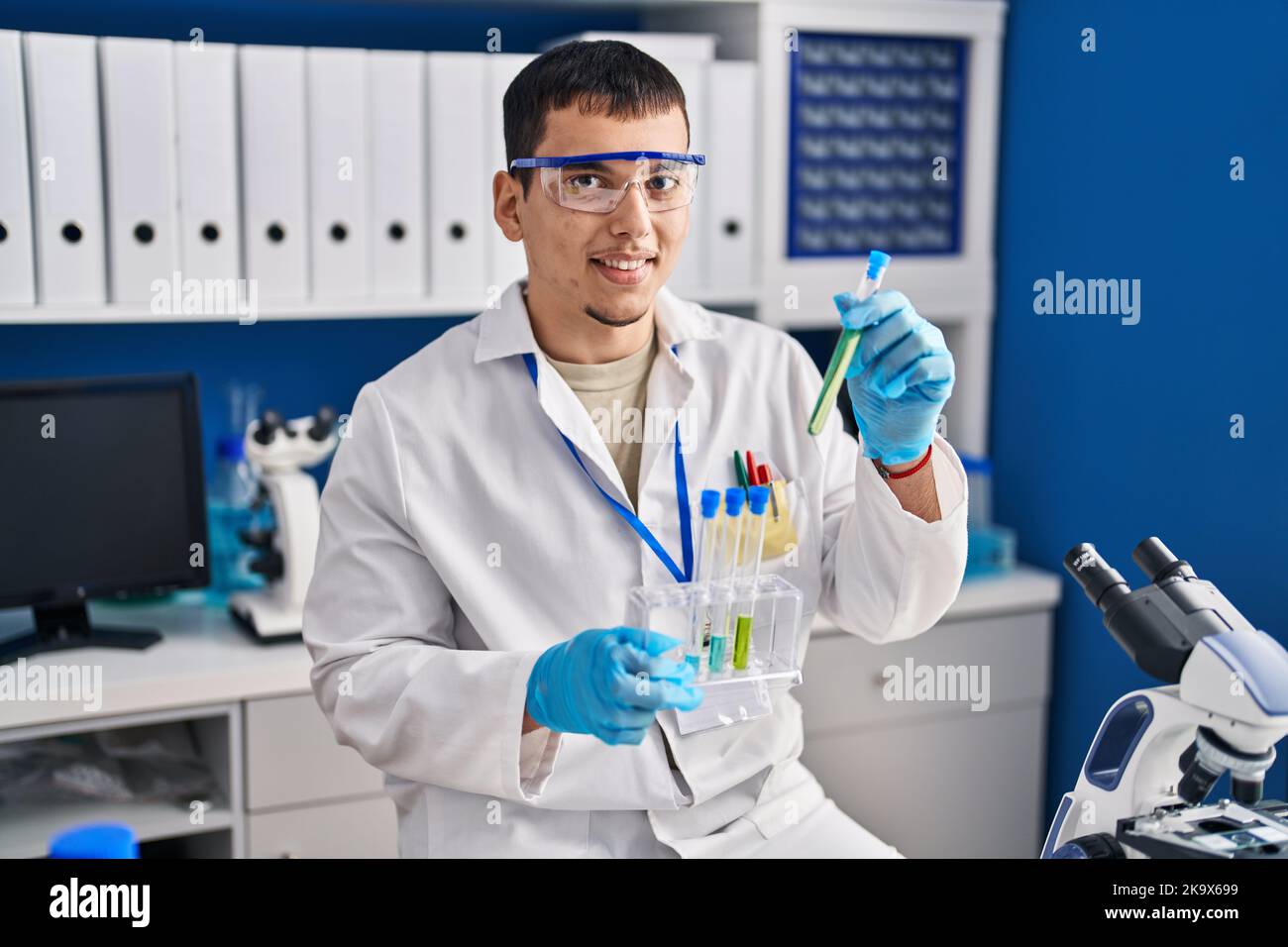 Young man scientist smiling confident holding test tubes at laboratory ...
