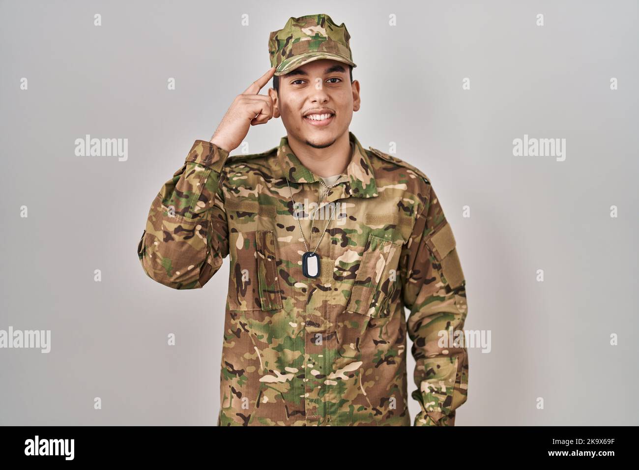 Young arab man wearing camouflage army uniform smiling pointing to head ...