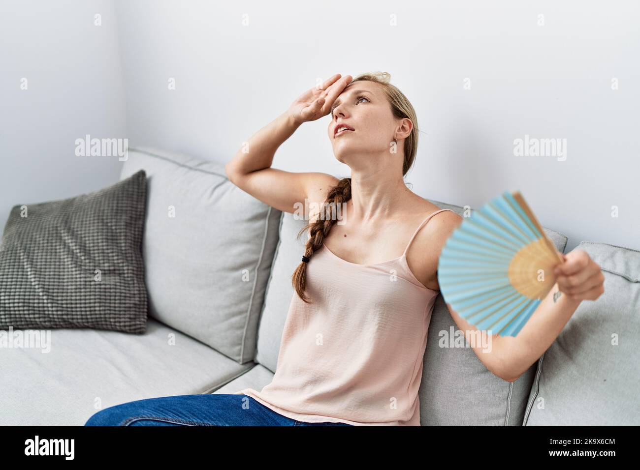 Young caucasian woman using hand fan sitting on sofa at home Stock ...