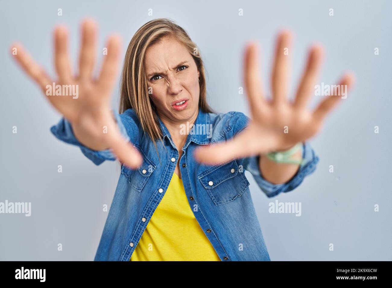 Young blonde woman standing over blue background afraid and terrified ...