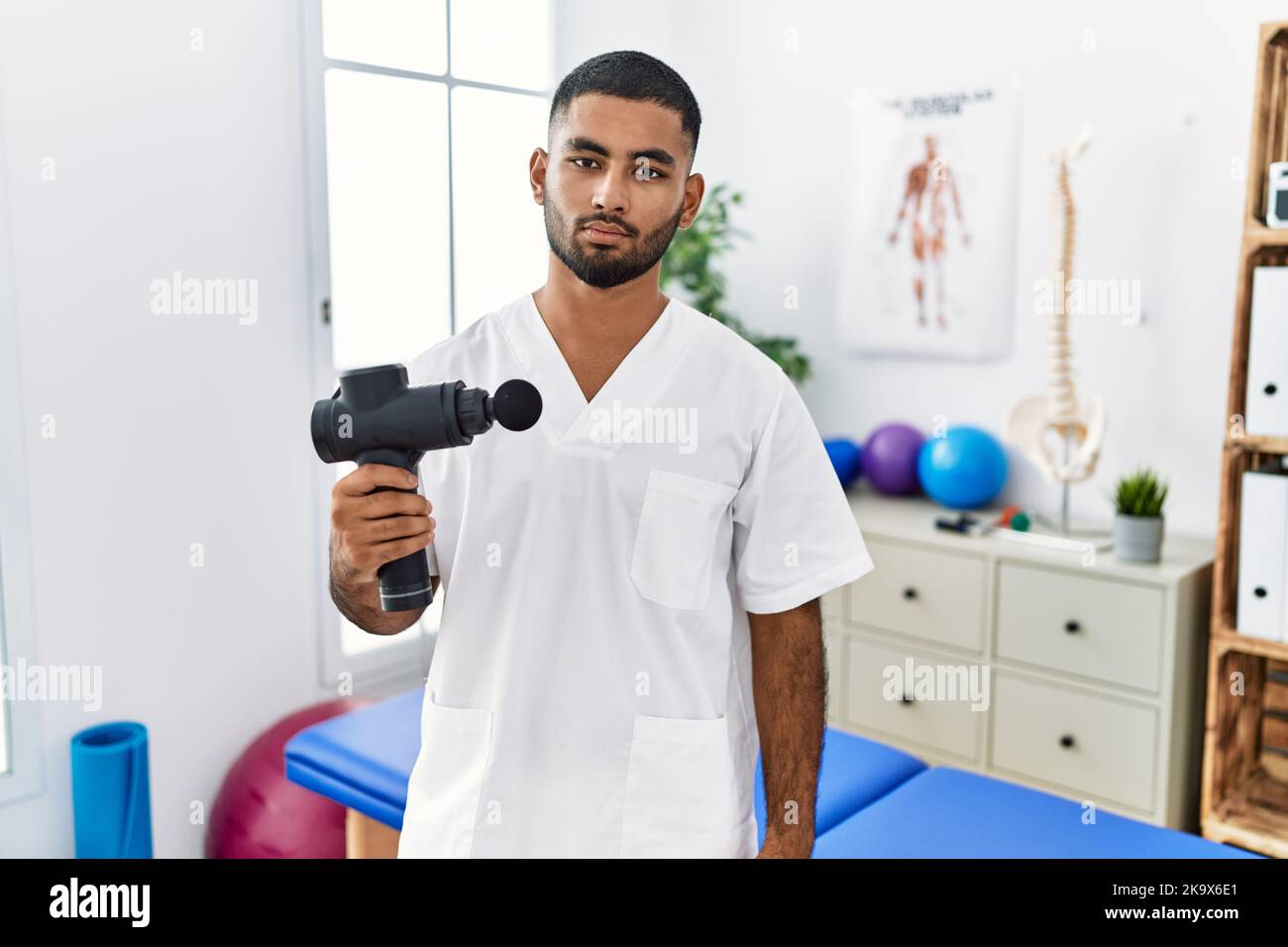 Young indian physiotherapist holding therapy massage gun at wellness ...