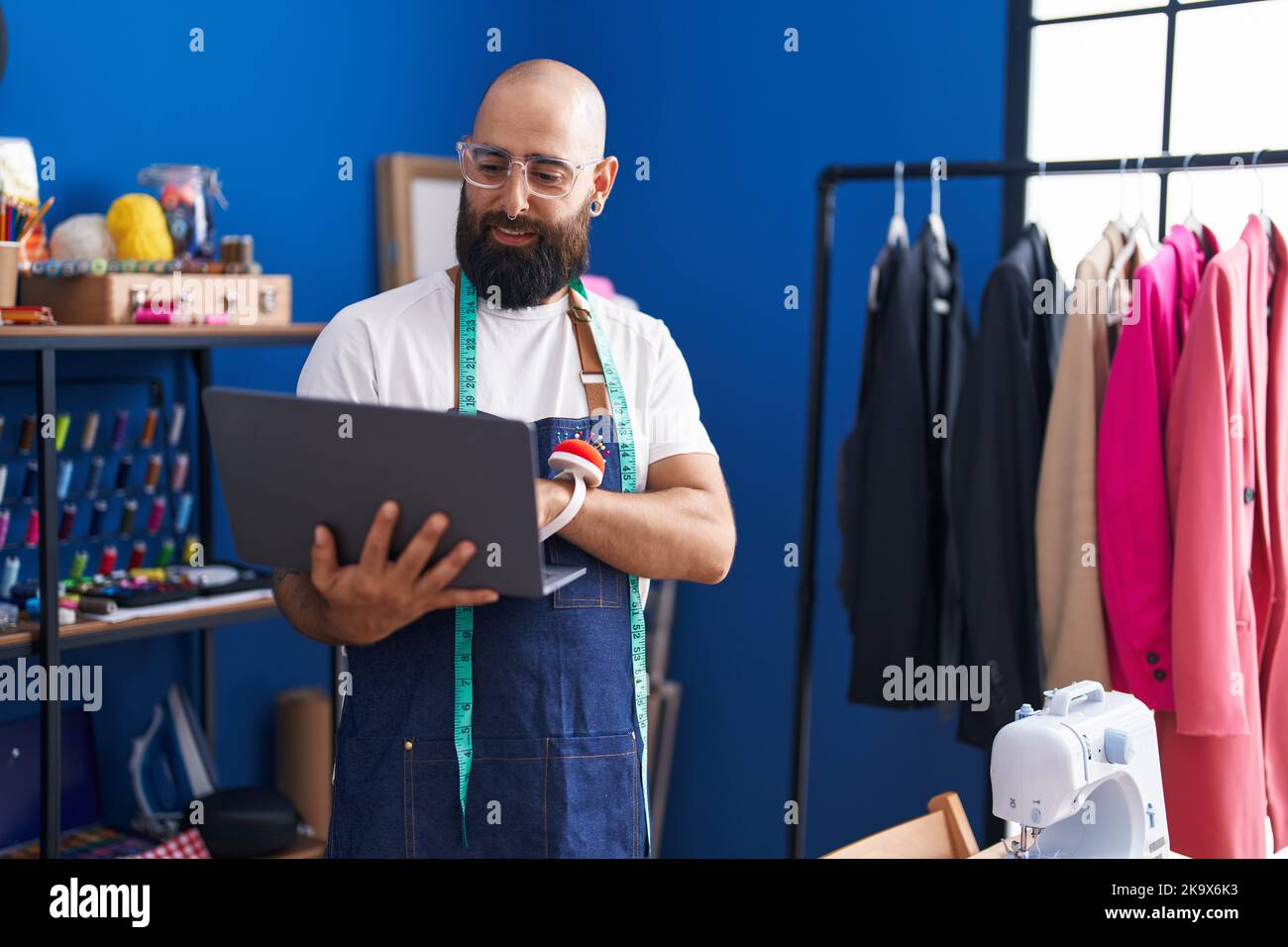 Young bald man tailor smiling confident using laptop at clothing ...