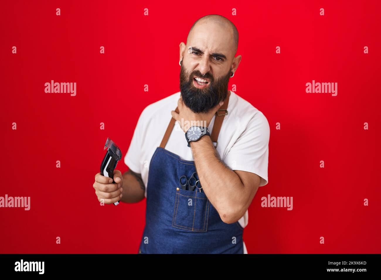 Young hispanic man with beard and tattoos wearing barber apron holding ...