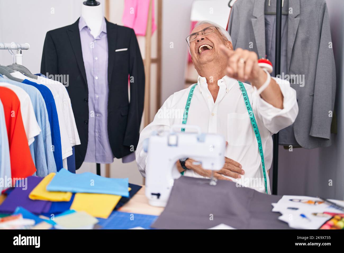 Middle age man with grey hair dressmaker using sewing machine laughing ...