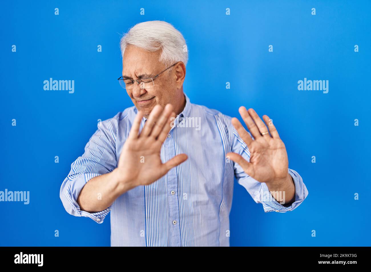 Hispanic Senior Man Wearing Glasses Moving Away Hands Palms Showing