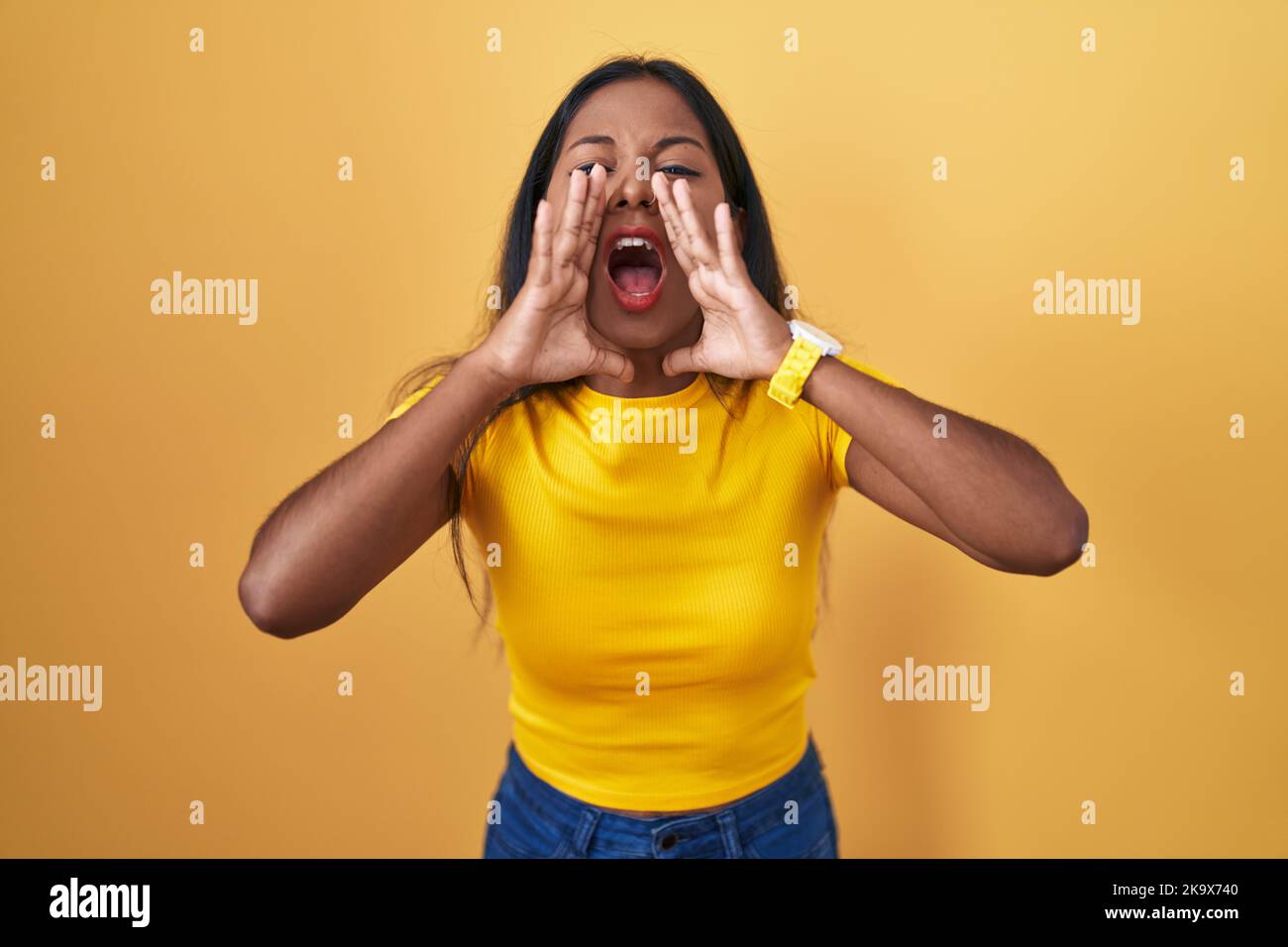 Young indian woman standing over yellow background shouting angry out ...