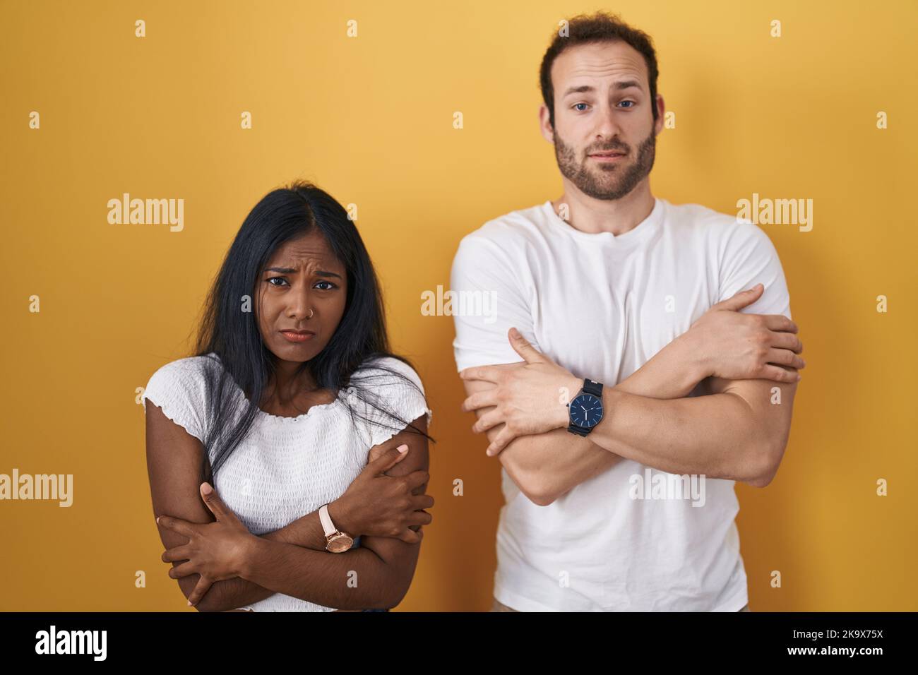 Interracial couple standing over yellow background shaking and freezing ...