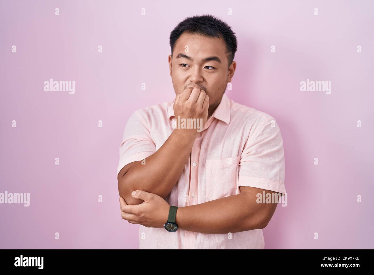 Chinese young man standing over pink background looking stressed and ...