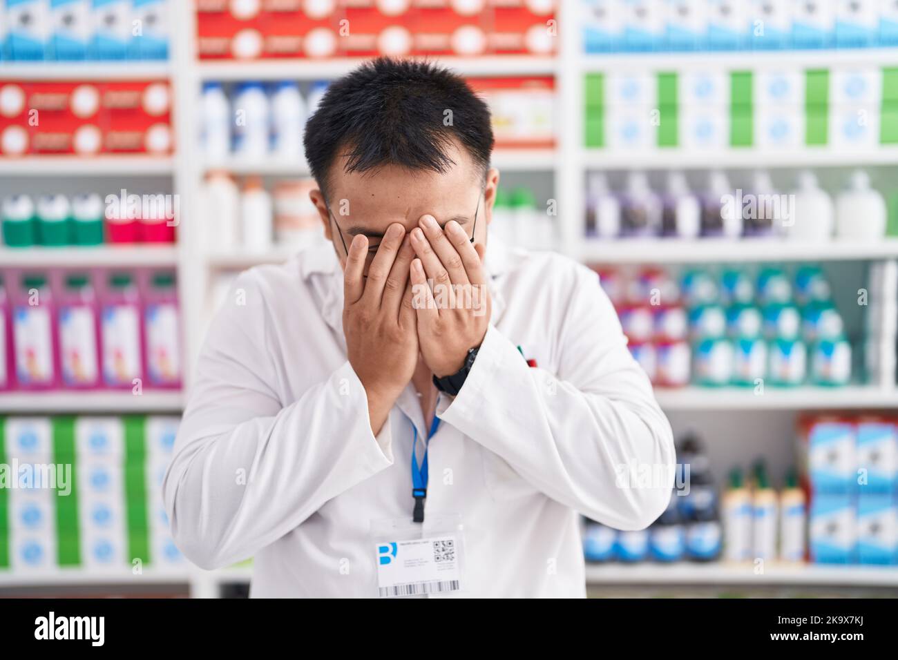Chinese young man working at pharmacy drugstore with sad expression ...