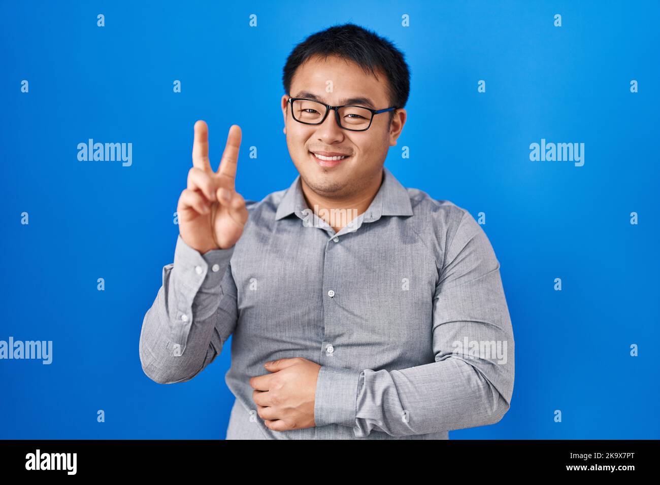 Young chinese man standing over blue background smiling with happy face ...