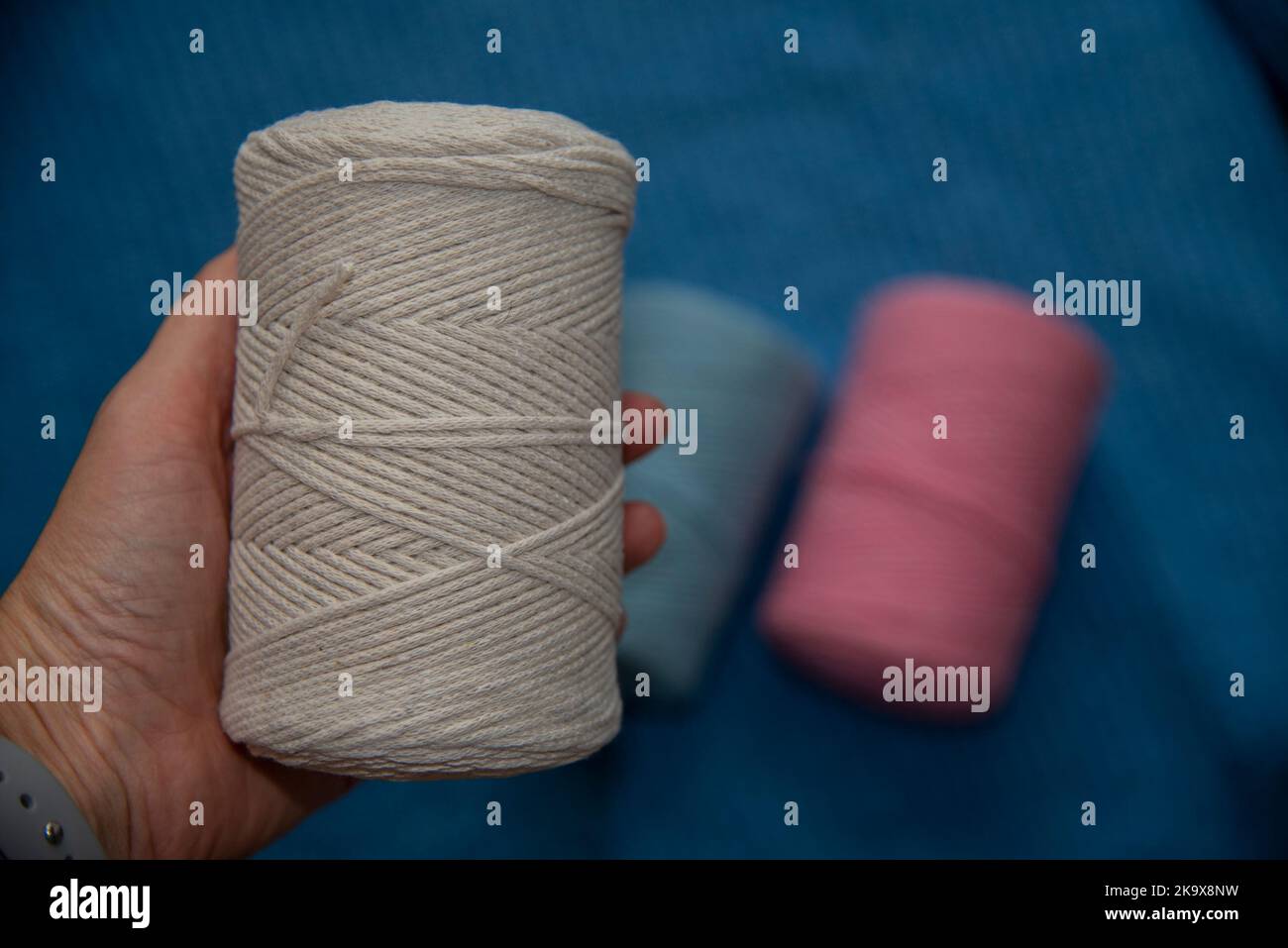 Coil of beige macrame thread in the hand on a blue backgraound Stock ...