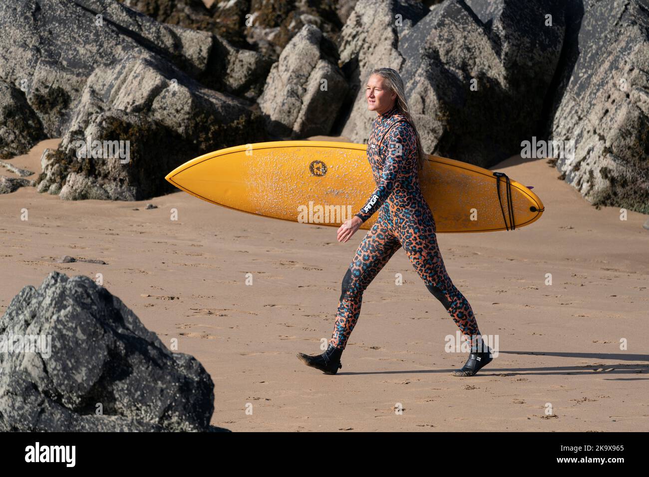 A female surfer in a brightly coloured wetsuit heads up the beach ...