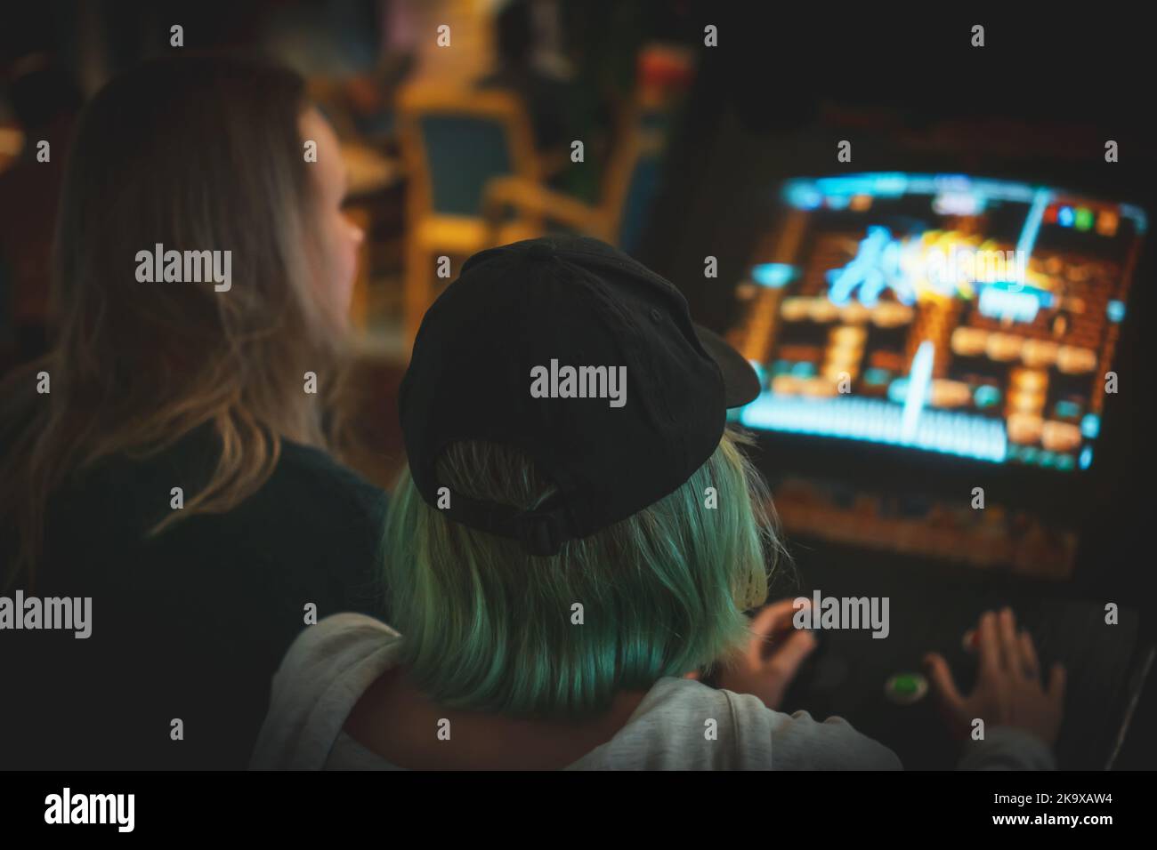 Two girls are playing arcade video game Stock Photo - Alamy