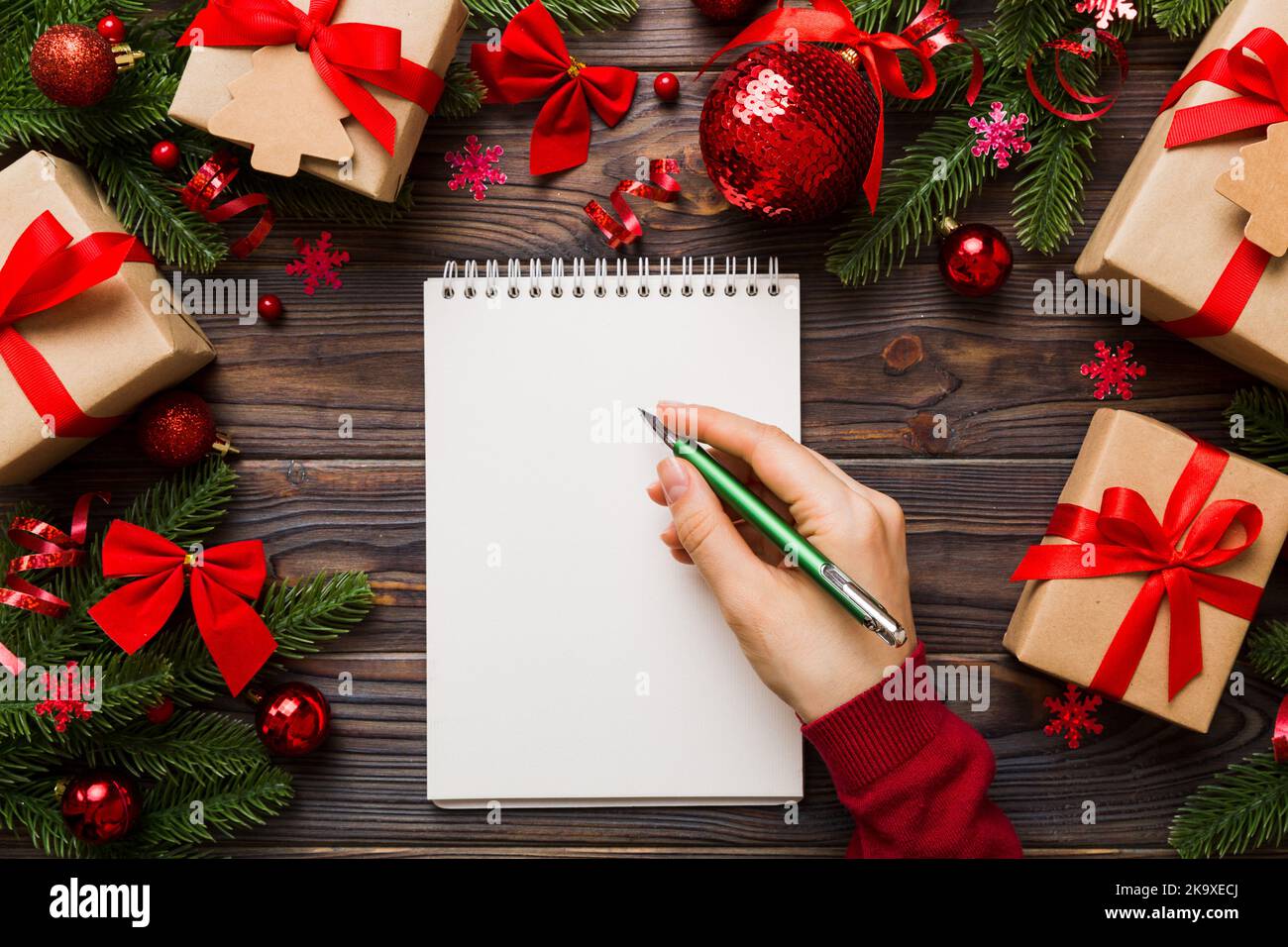 Woman writing Christmas to do list on notebook on colored background ...