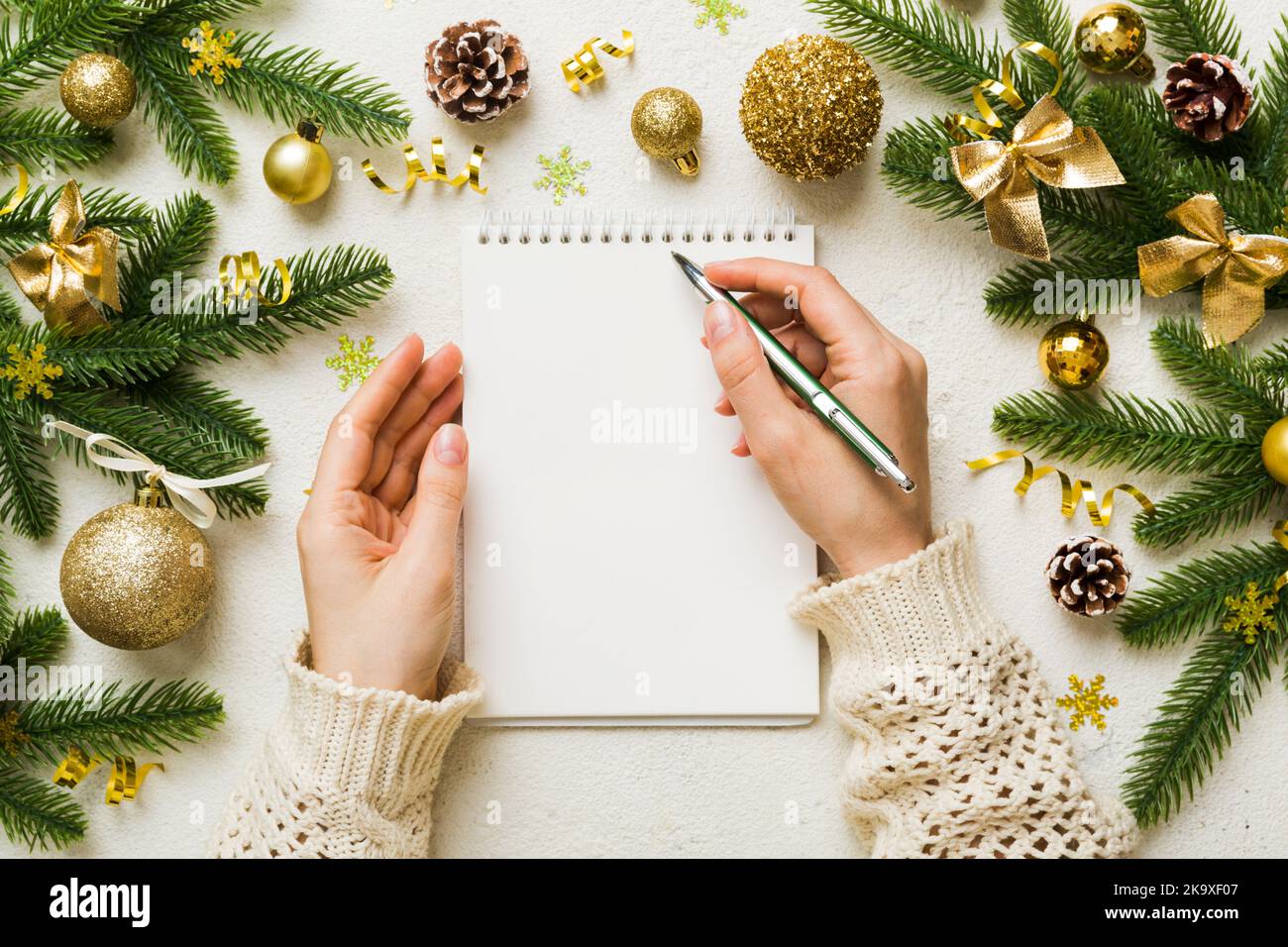 Woman writing Christmas to do list on notebook on colored background ...